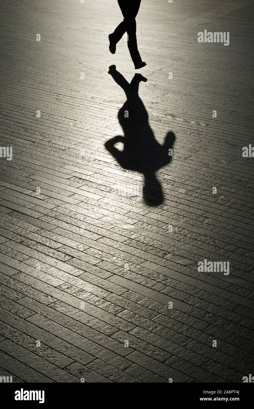 Silhouette and shadow of a jogger running across modern paving blocks ...