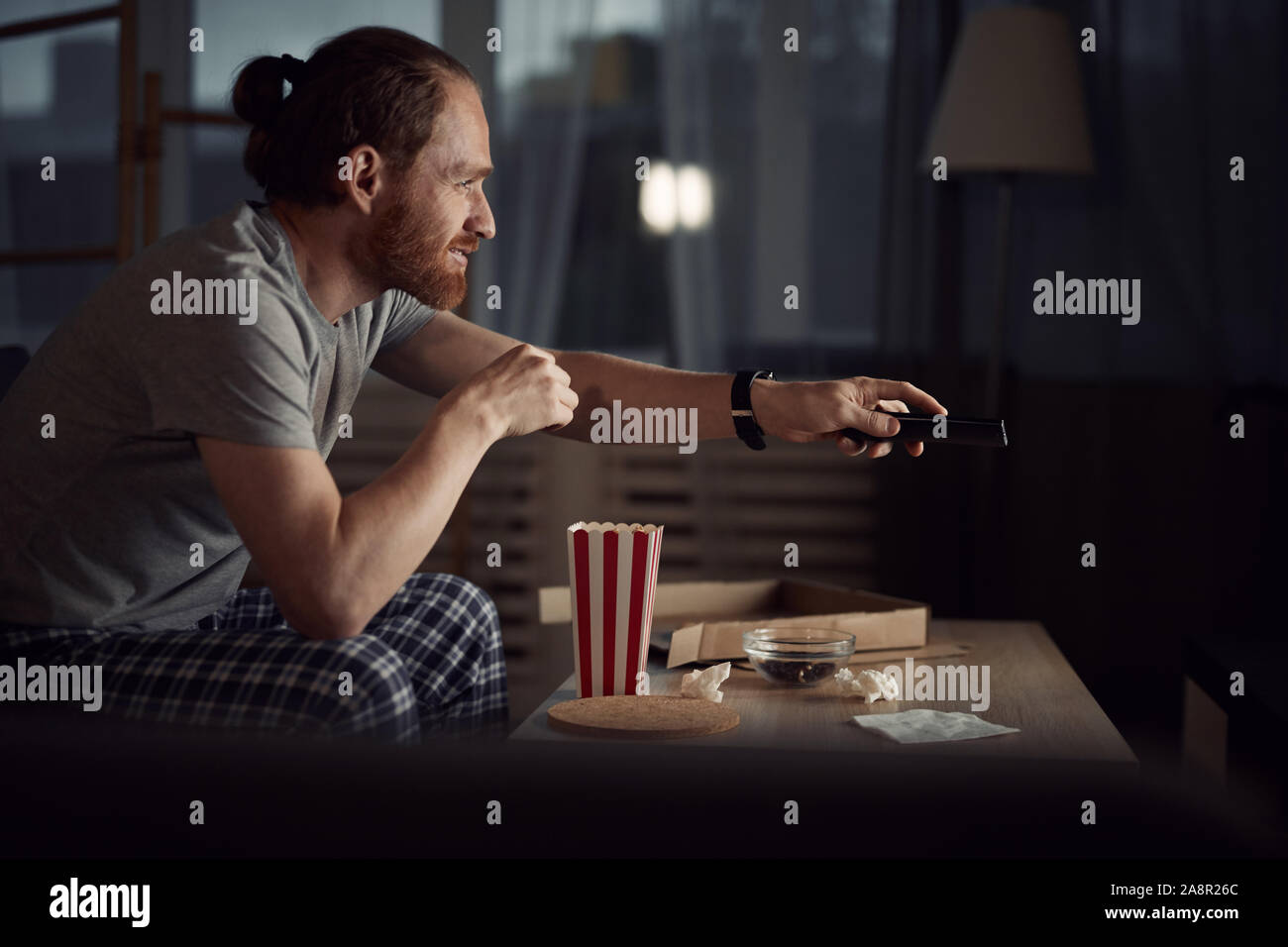 Side view portrait of contemporary man watching TV in dark and eating ...