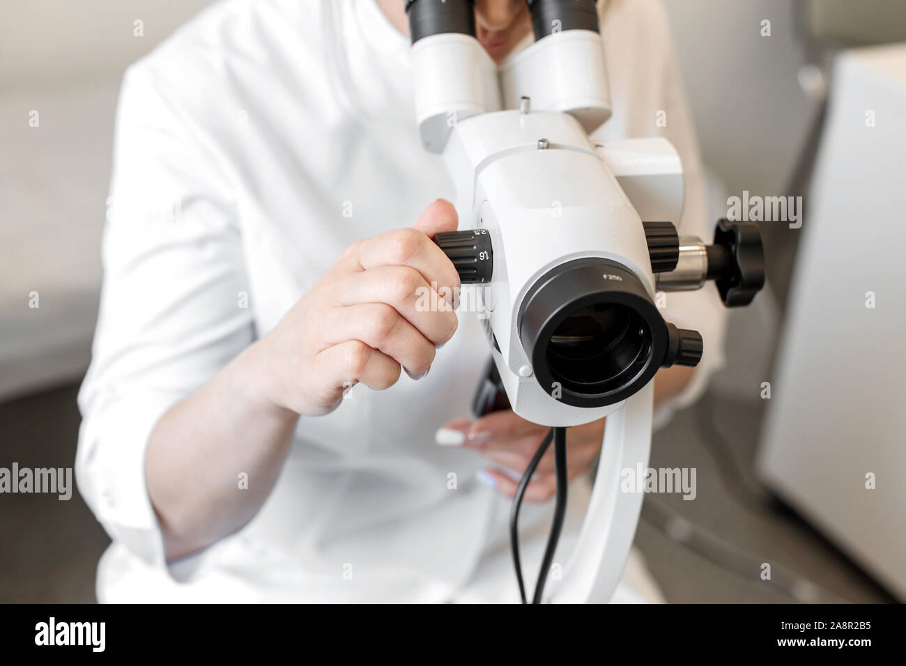 Female blond doctor gynecologist looks through a colposcope ...