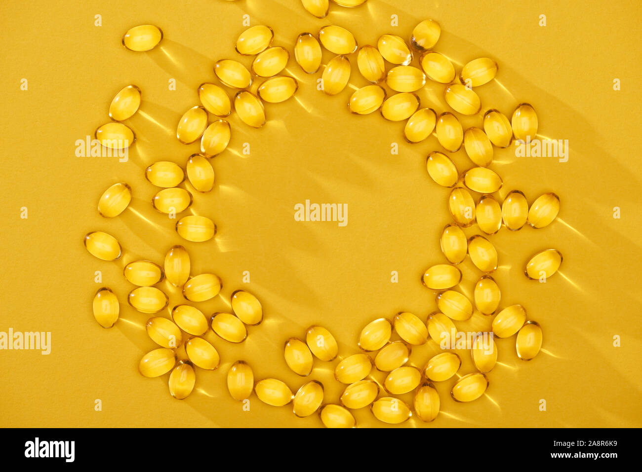 top view of golden shiny fish oil capsules arranged in circle on yellow ...