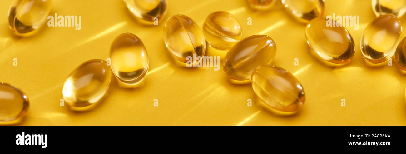 close up view of golden shiny fish oil capsules scattered on yellow ...