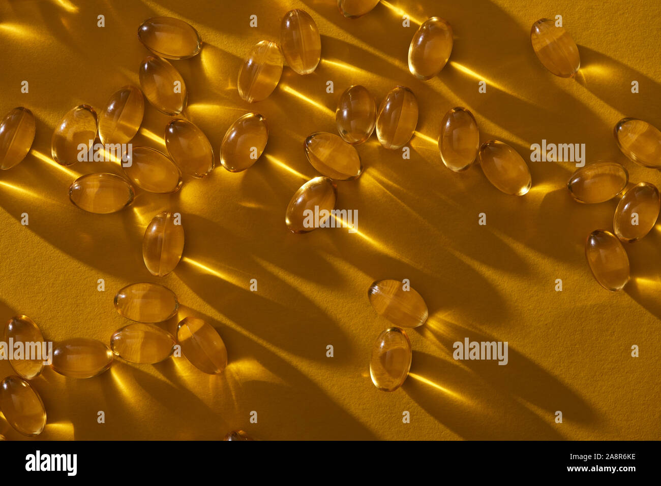 golden shiny fish oil capsules scattered on yellow background in dark ...