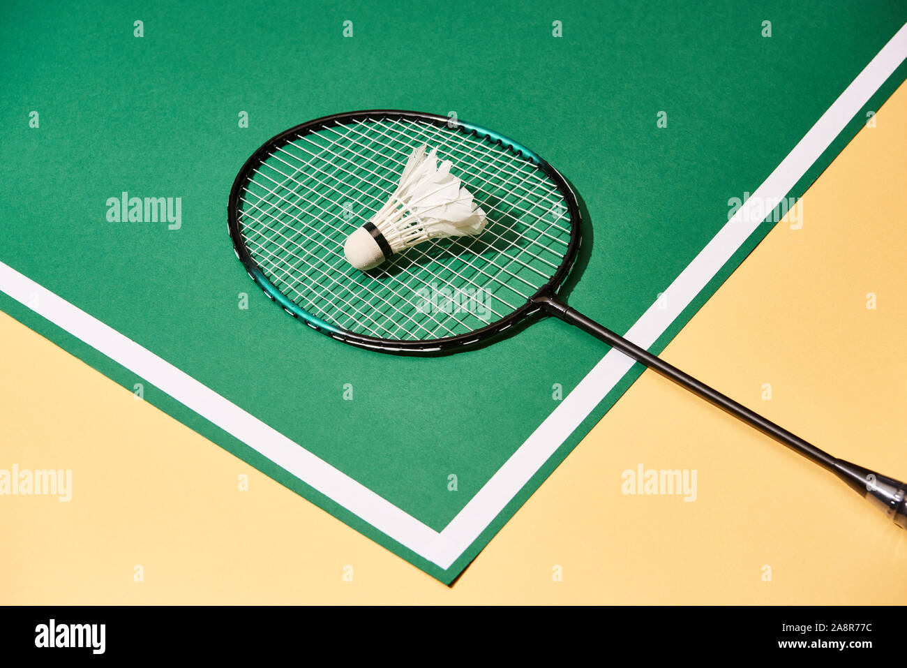 Metal badminton racket and shuttlecock on green and yellow surface with ...