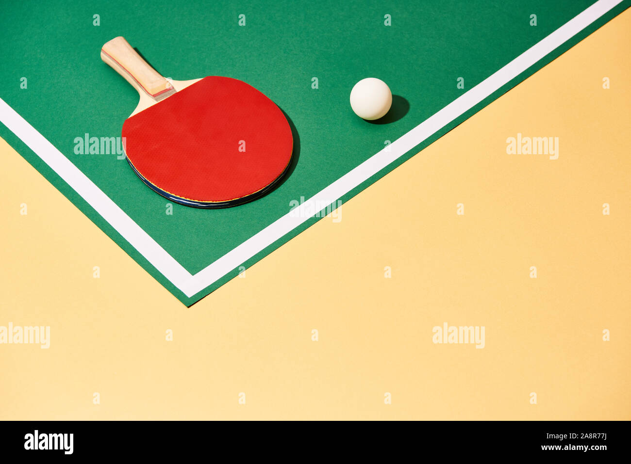 Table tennis racket and ball on green and yellow surface with white ...