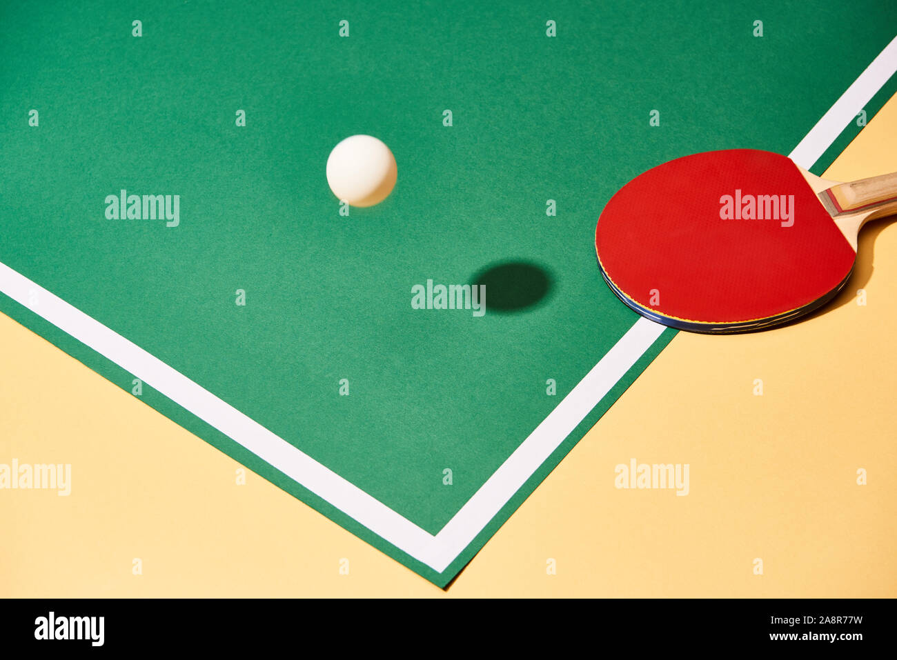 Red table tennis racket and ball on paying table and yellow surface ...