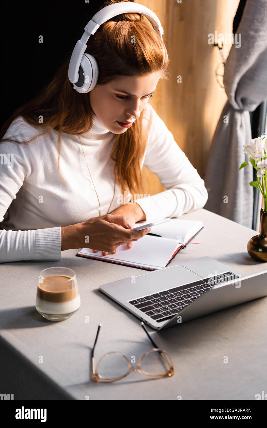 concentrated woman in headphones writing in notepad while watching ...