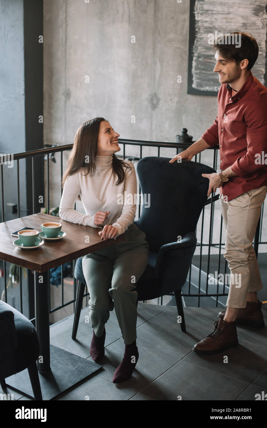 smiling woman looking at man pushing chair on balcony in coffee shop ...