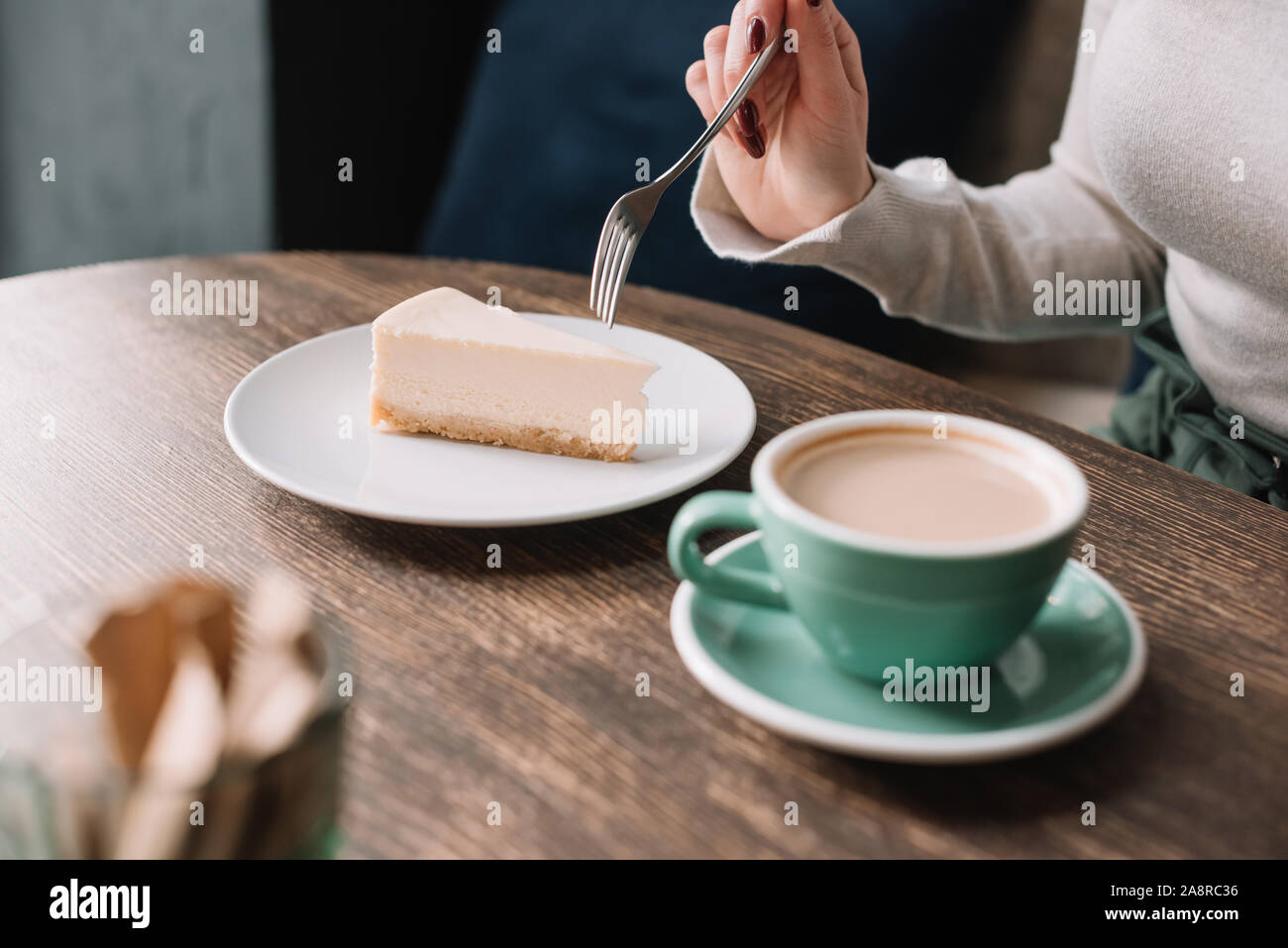 partial view of woman eating cheesecake with fork and drinking coffee ...