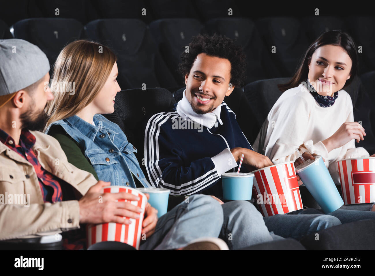 multicultural friends sitting, smiling and talking in cinema Stock ...