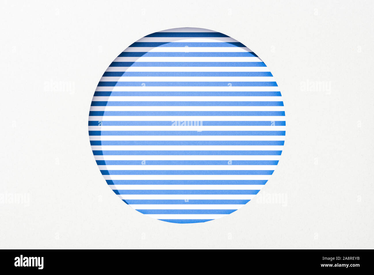 cut out round hole in white paper on blue and white striped background ...