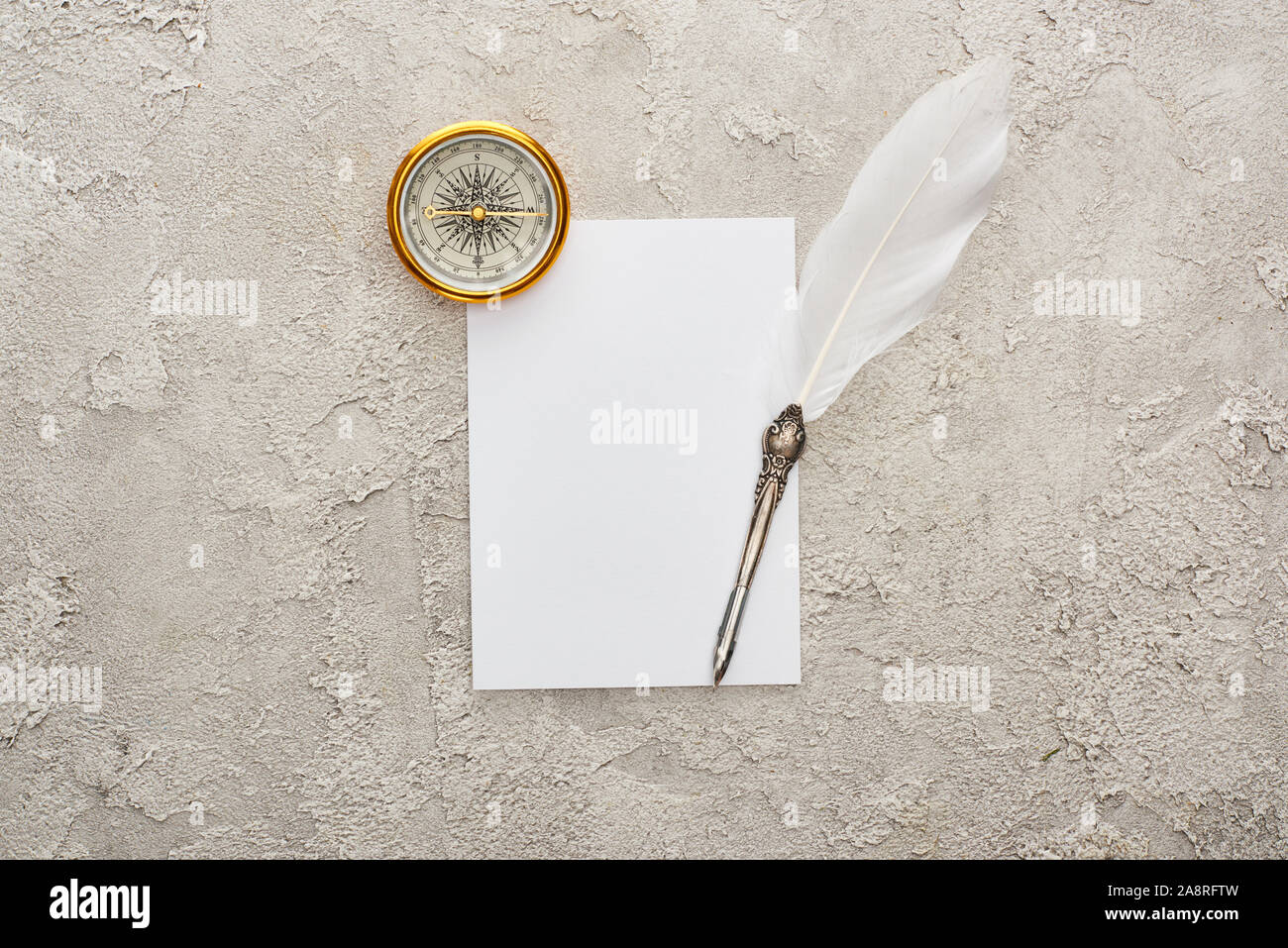 top view of quill pen on white card near golden compass on grey ...