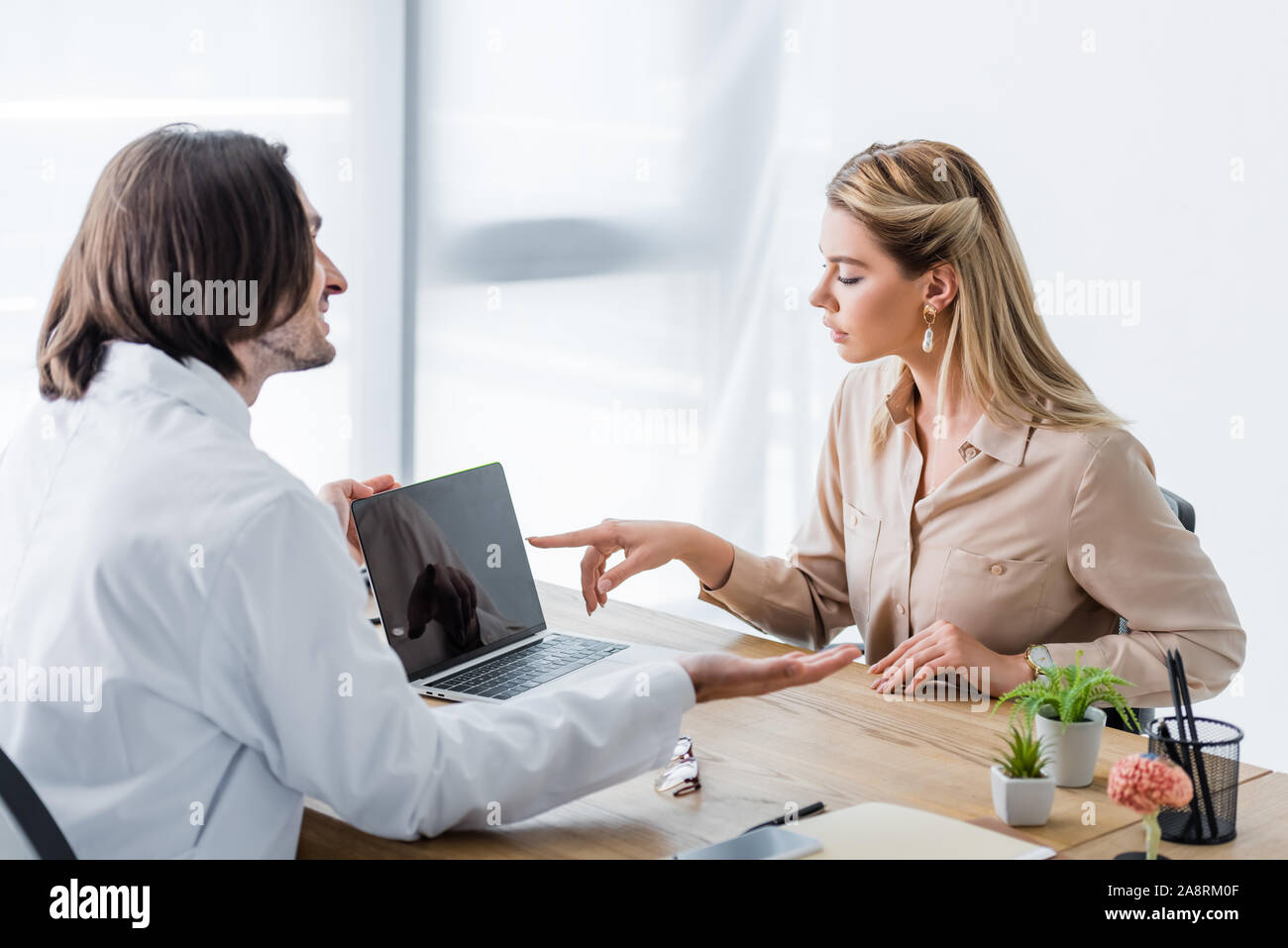 patient sitting with doctor behind wooden table and pointing with ...