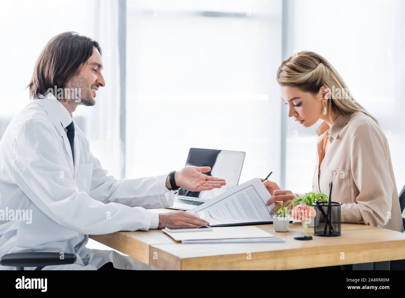 woman signing insurance claim form during appointment with doctor in ...