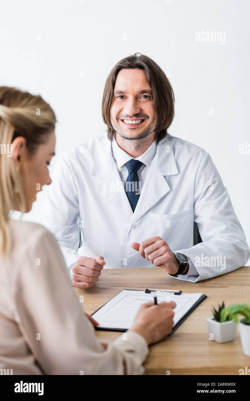patient sitting with doctor behind wooden table and signing document ...
