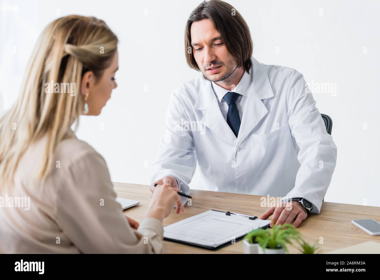 patient sitting with doctor behind wooden table and signing document ...