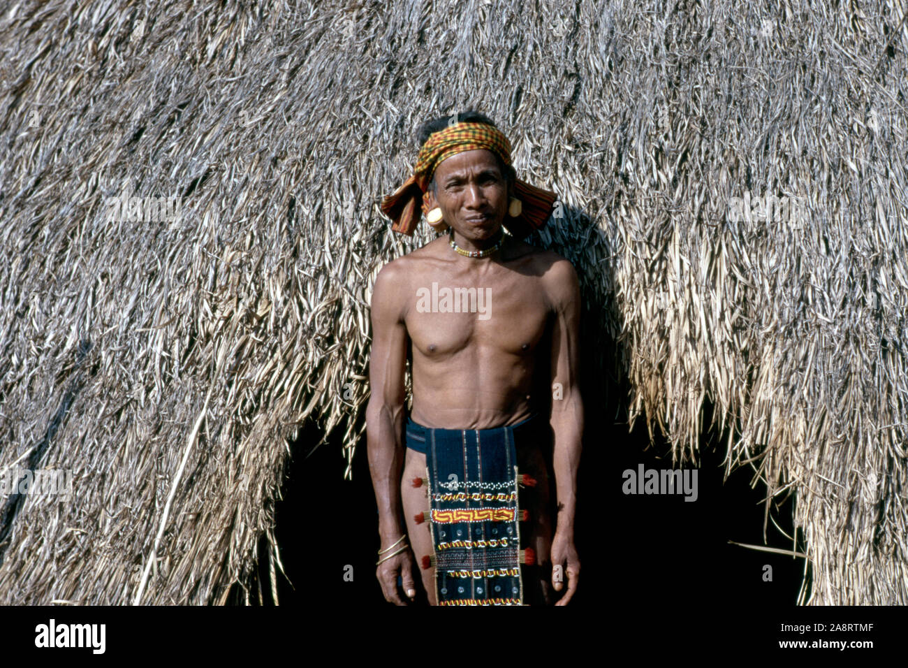 An indigenous Mnong (Pnong) man standing outside his house wearing ...