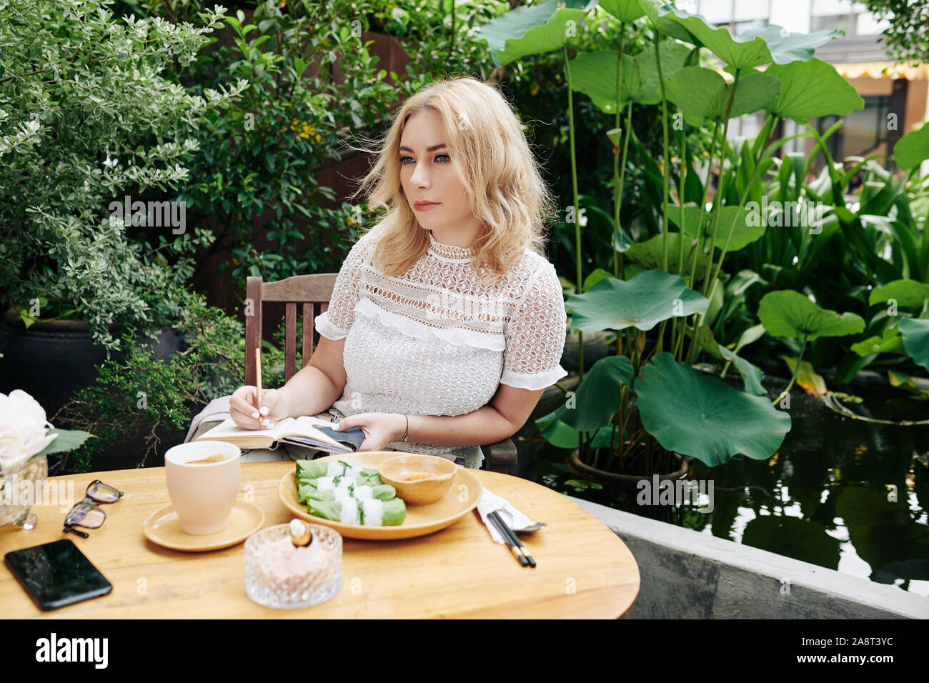 Pensive female entrepreneur eating business lunch and writing thoughts ...
