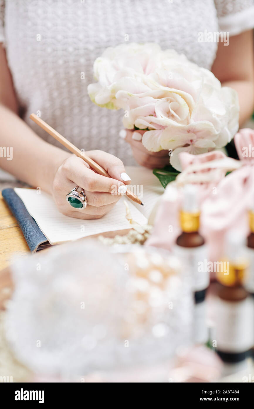 Hands of woman with light pink flower in hand writing ideas for next ...