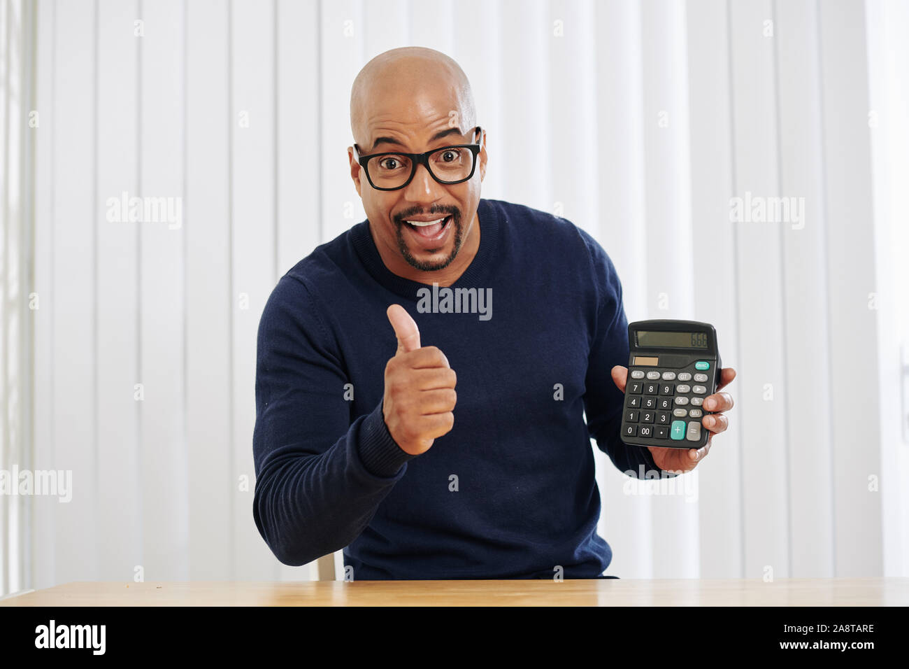Portrait of happy excited man holding calculator and showing thumbs-up ...