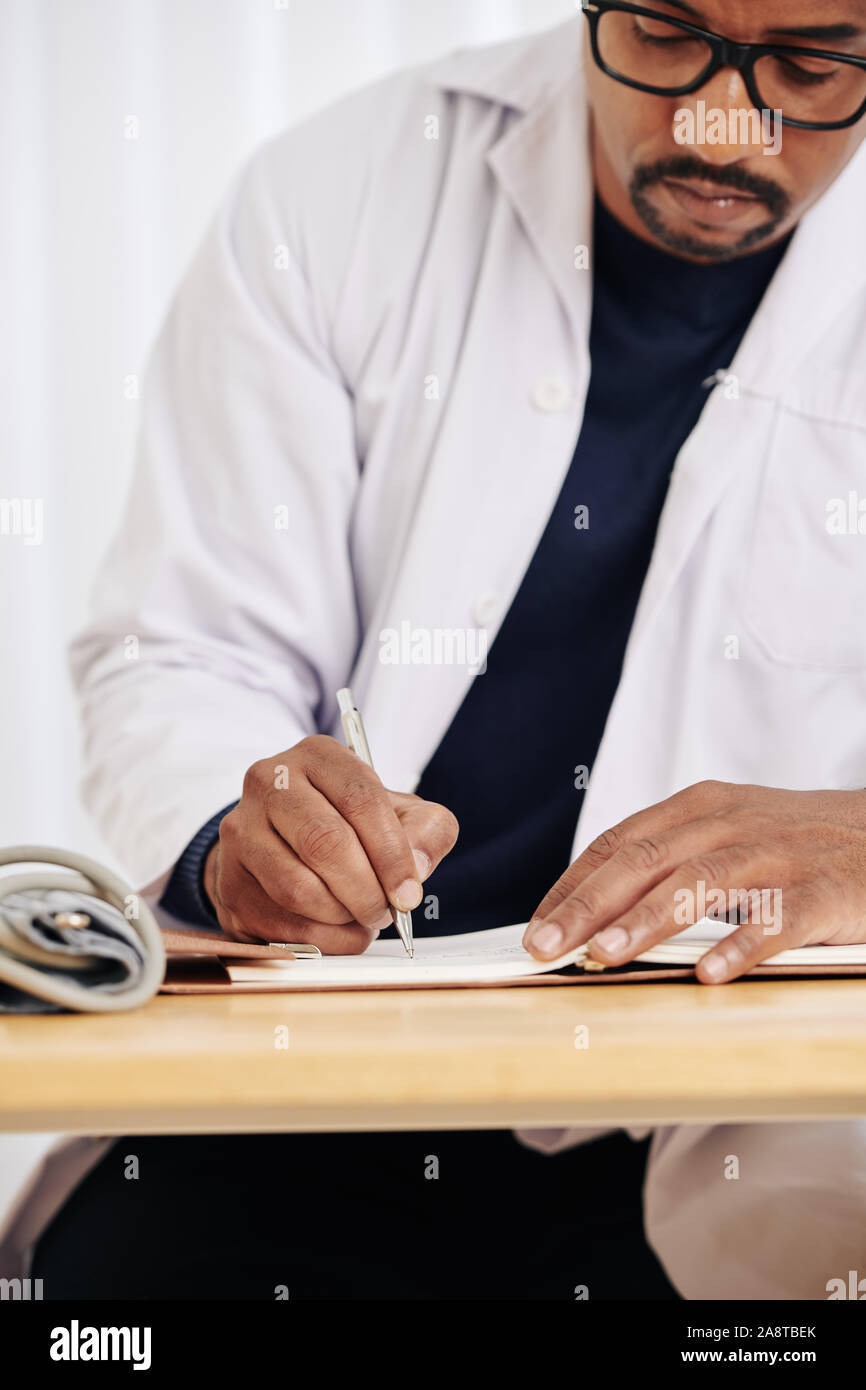 Serious general pracitioner sitting at office desk and writing ...