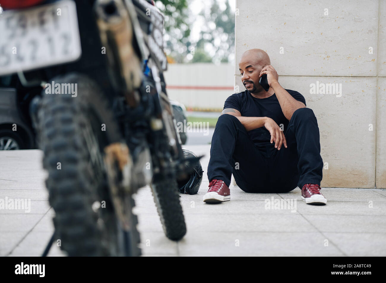 Handsome mixed-race man sitting on ground and calling mechanic as his ...