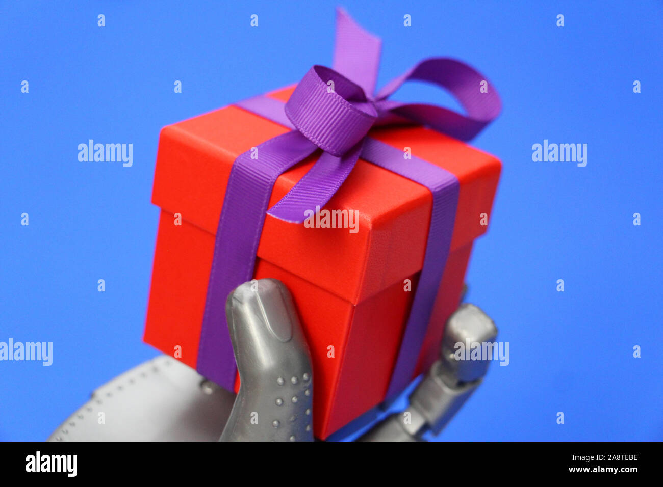 Robot hand holds a gift. Red gift box tied with a purple bow. Smart ...