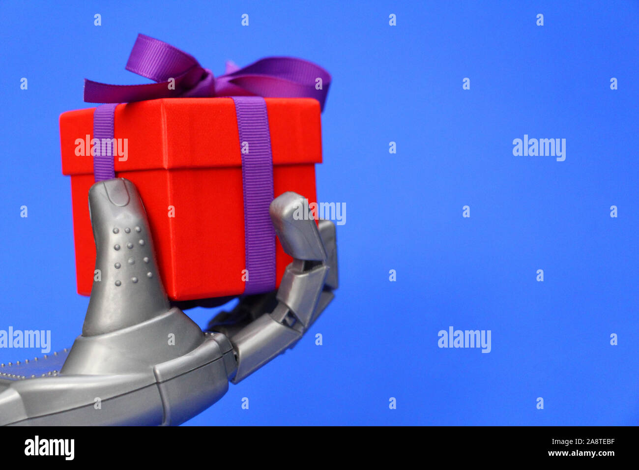 Robot hand holds a gift. Red gift box tied with a purple bow. Smart ...