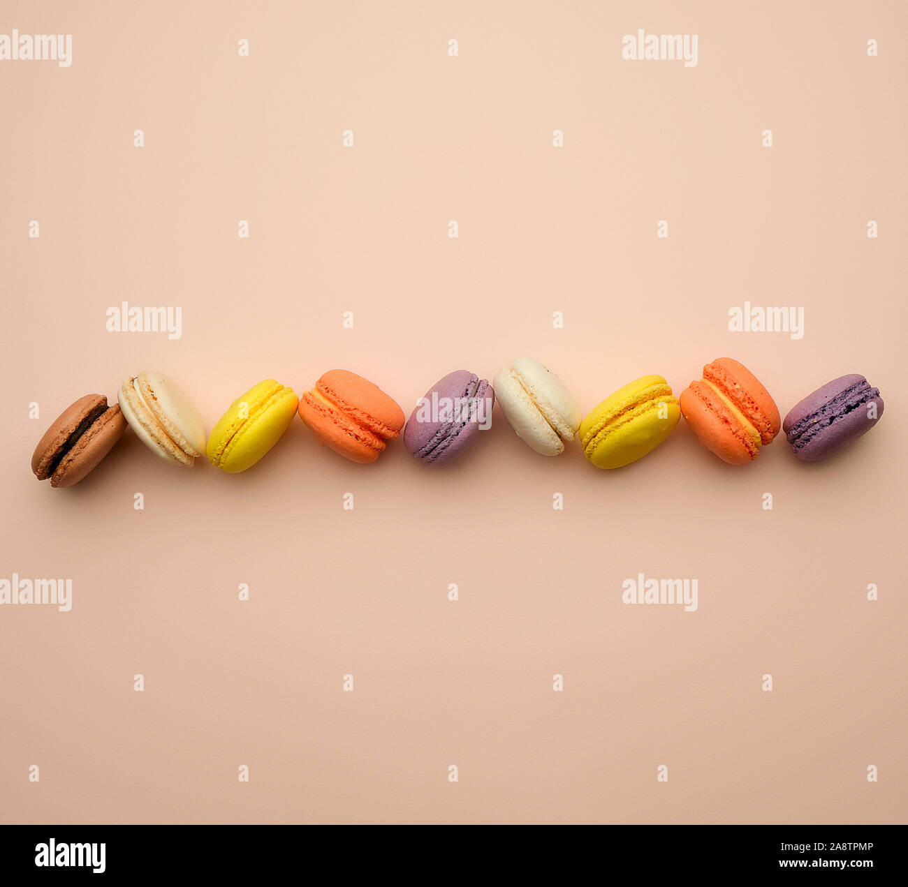 round multi-colored baked macarons with cream lie in a line on a beige background, flat lay ...