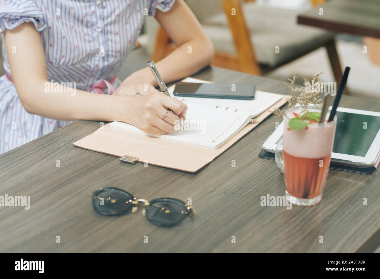Hands of young woman filling planner when sitting at table in small ...