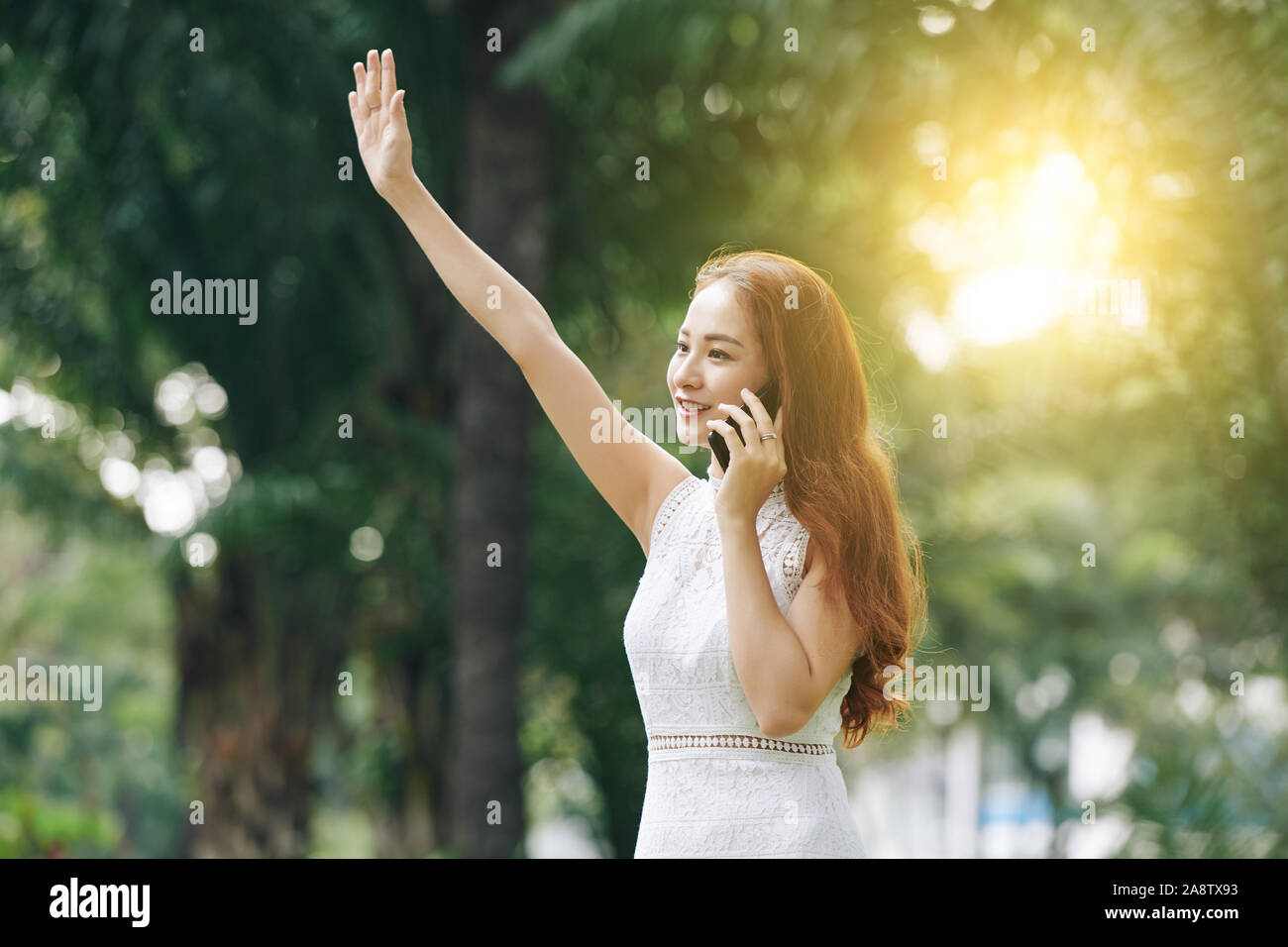 Attractive young Vietnamese woman talking on phone and waving with her ...