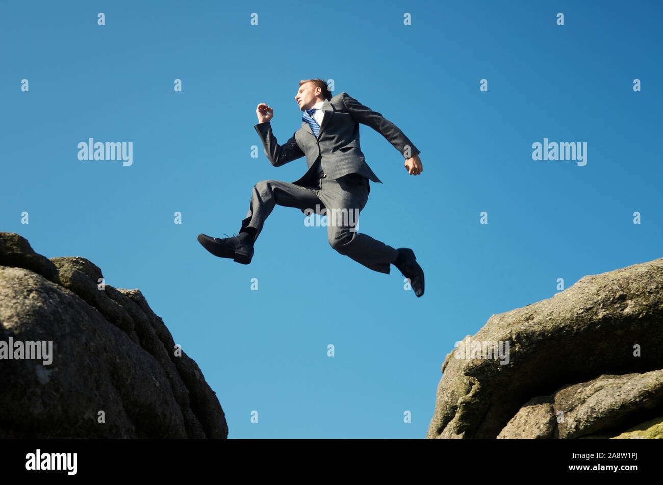 Brave businessman taking a daring leap between two boulders outdoors ...