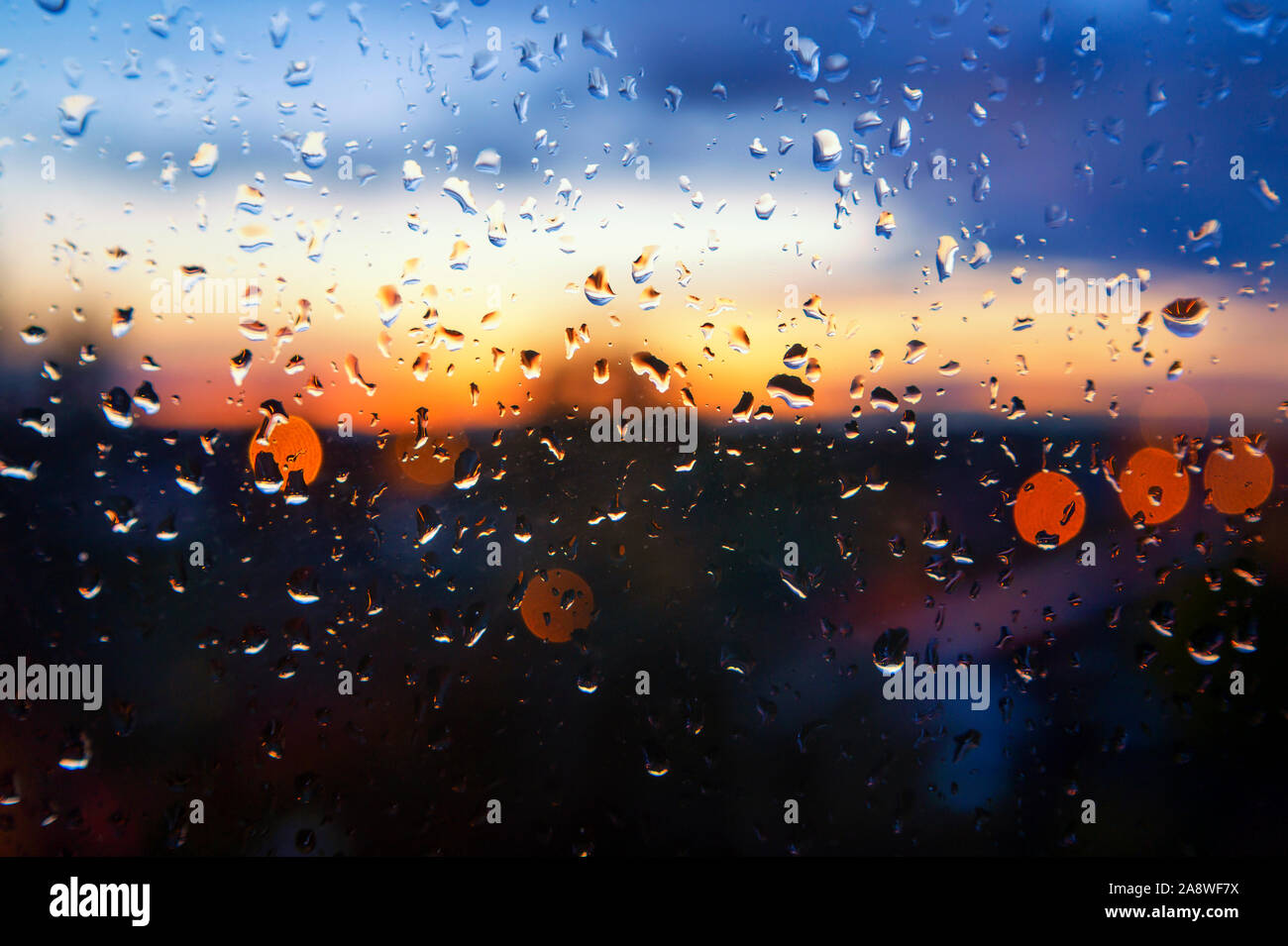 Colorful sunset through wet window glass with beaded raindrops and rivulets of water on a stormy ...