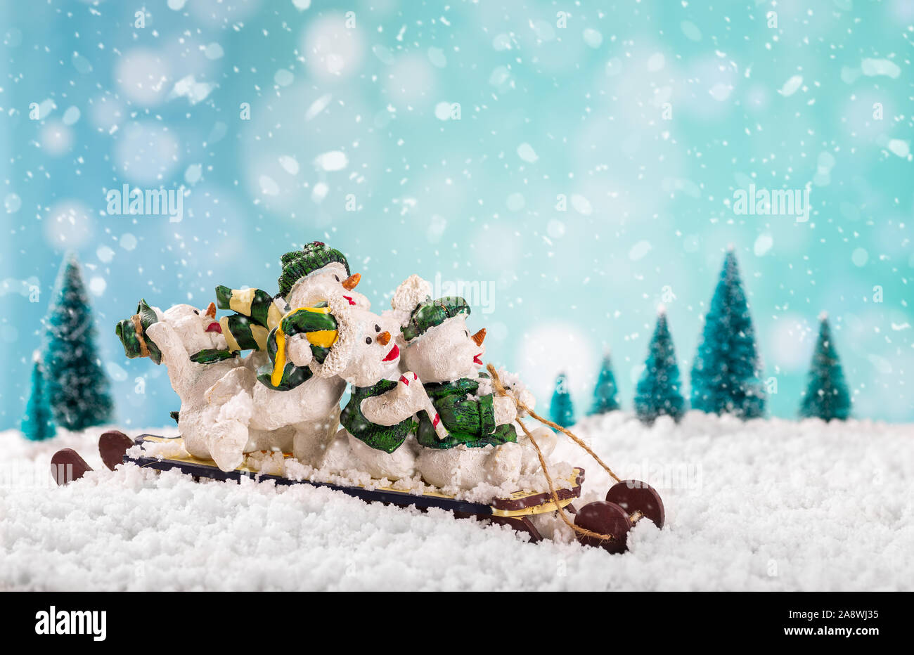 Snowmen figurines on a sled with falling snow against a bright colorful ...