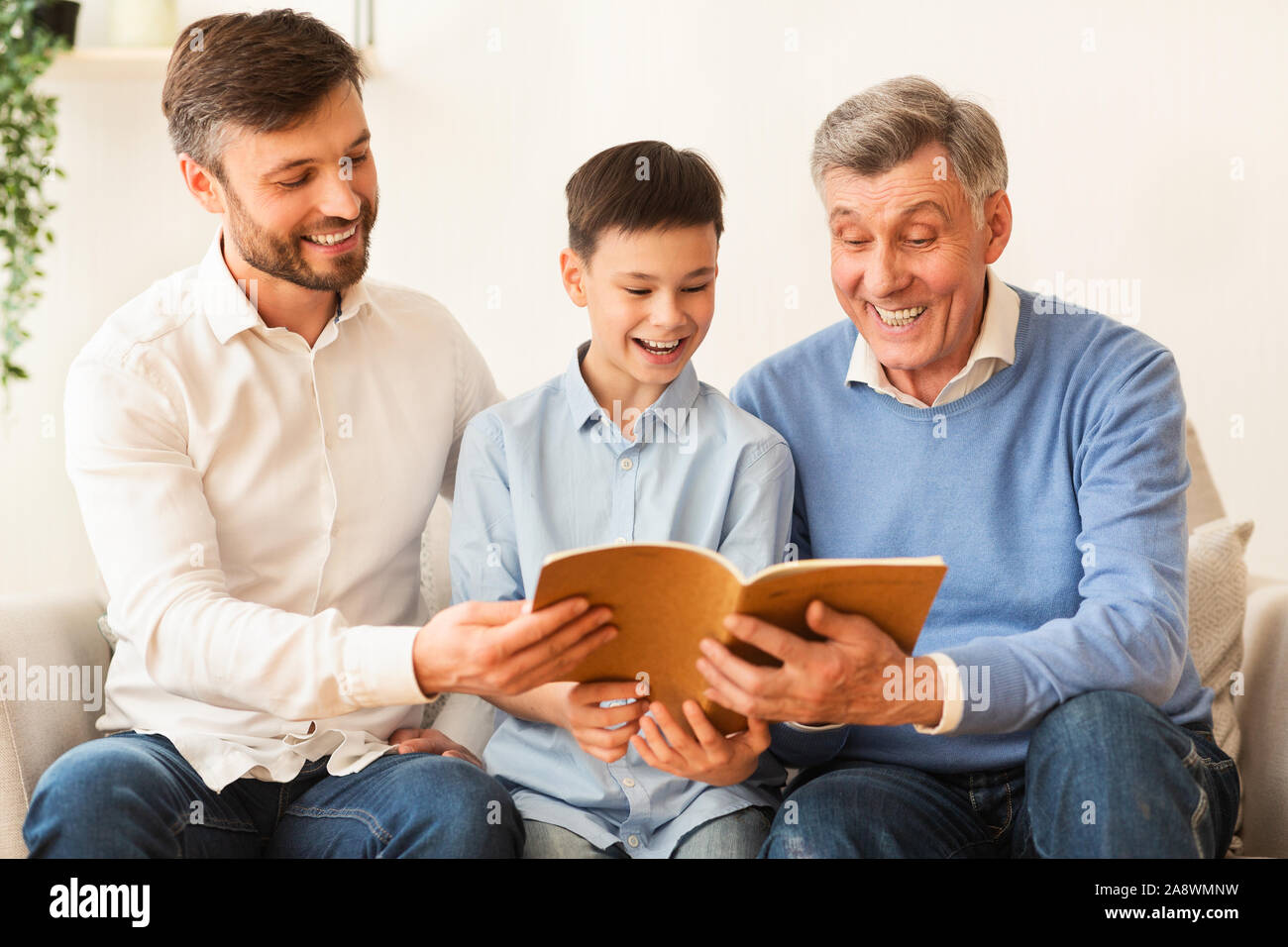 Happy Boy Reading Book With Dad And Grandpa At Home Stock Photo - Alamy
