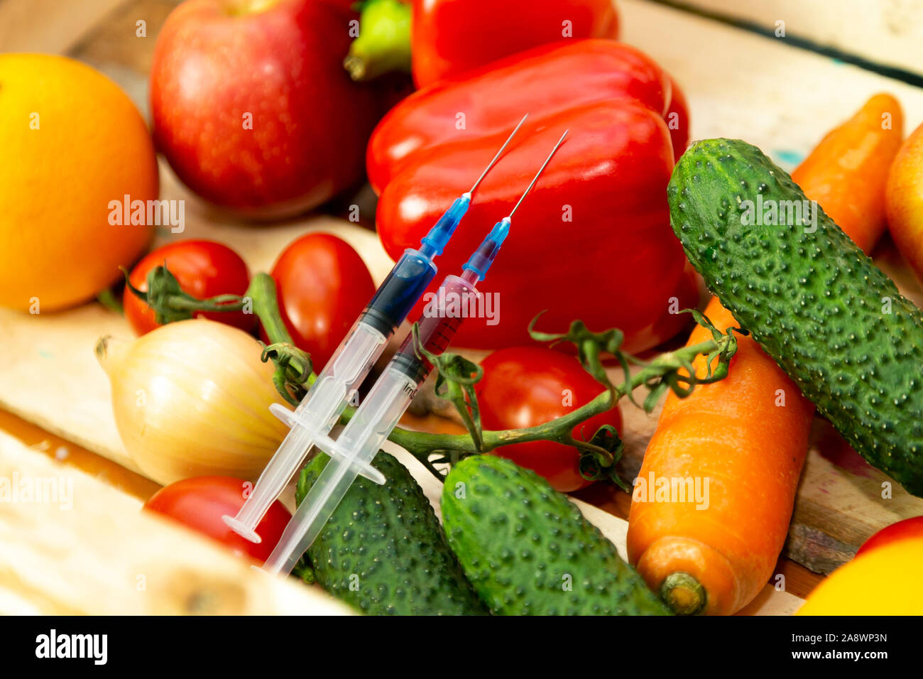 Two syringes with nitrates and pesticides lie on box vegetables and ...