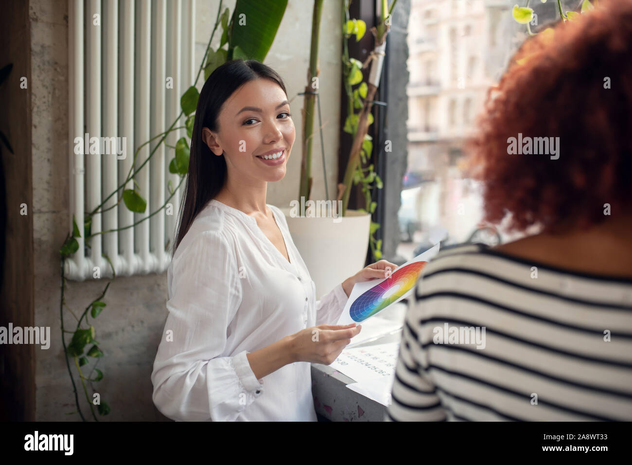 Designer holding color palette while sitting near friend Stock Photo ...