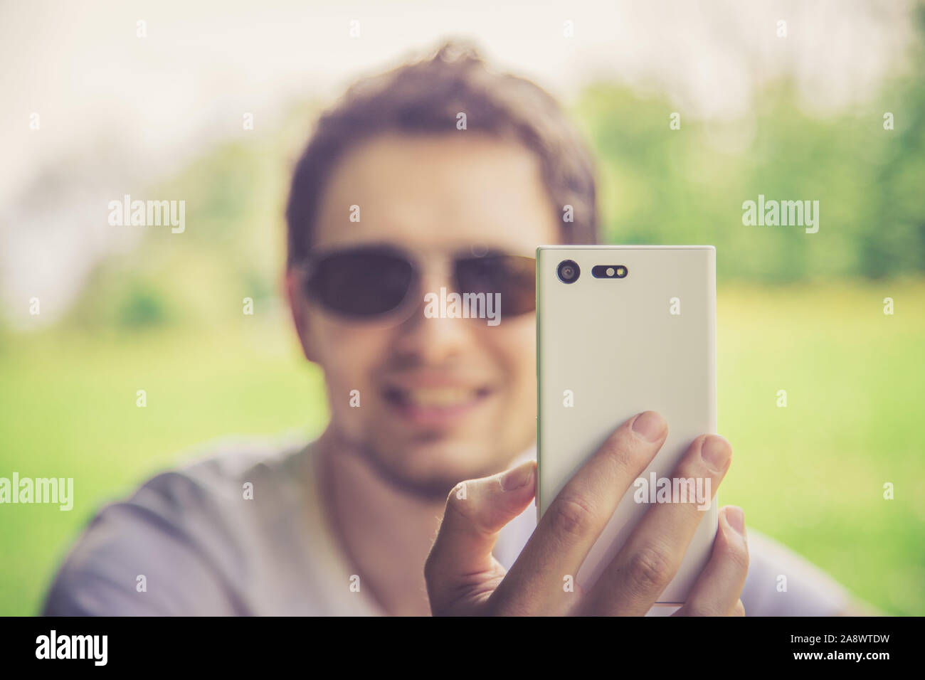 Man is taking a picture with his mobile phone, outdoors in the park ...