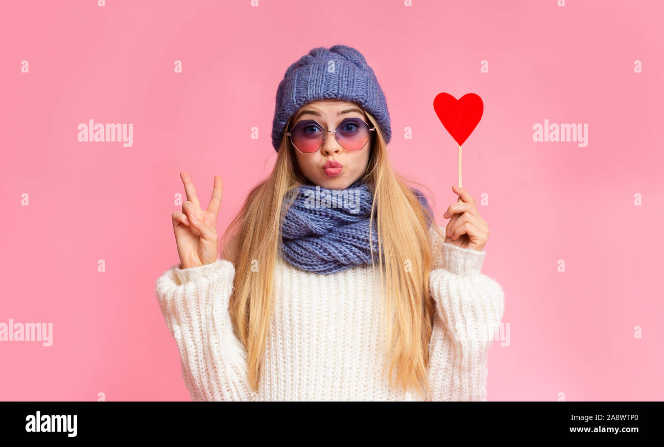 Cute girl showing peace sign, holding red heart card Stock Photo - Alamy