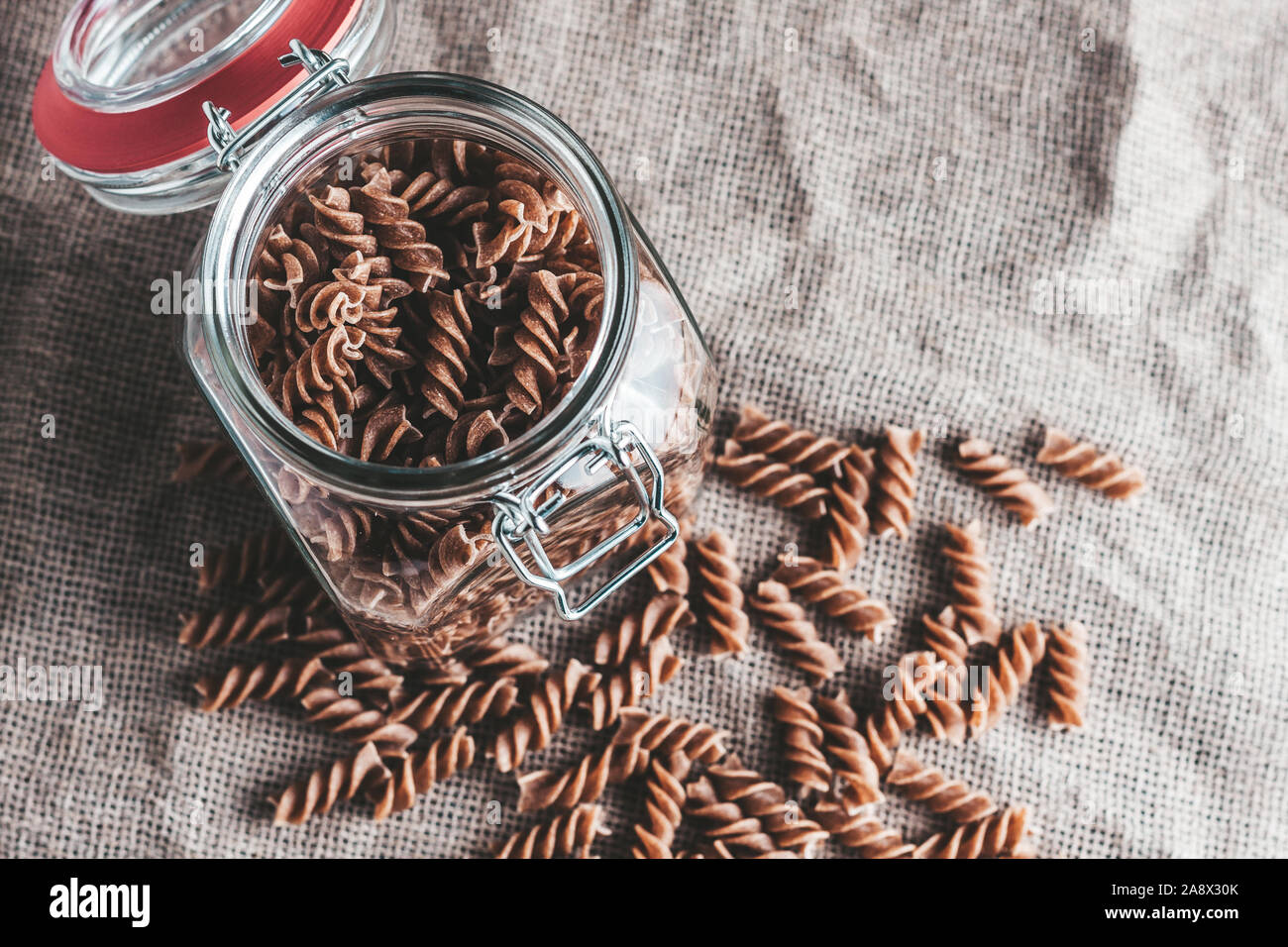 Dark brown whole grains of pasta in a glass jar close up - top view ...