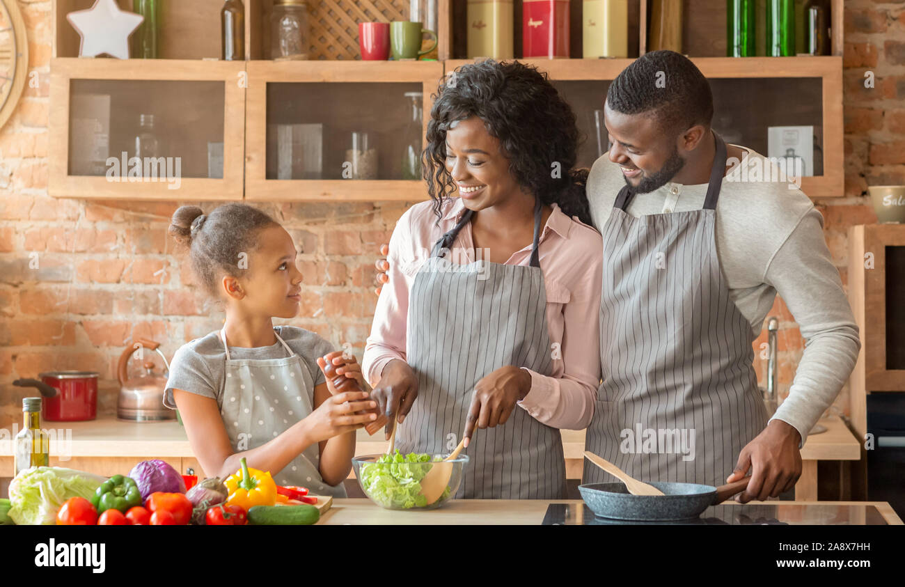 Afro girl seasoning veggies salad, cooking with parents Stock Photo - Alamy