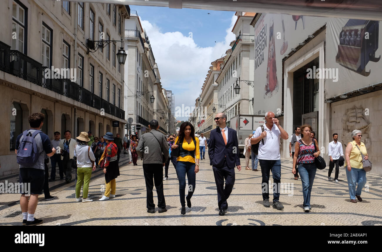 Tourists and local people smiling and walking down a picturesque street ...