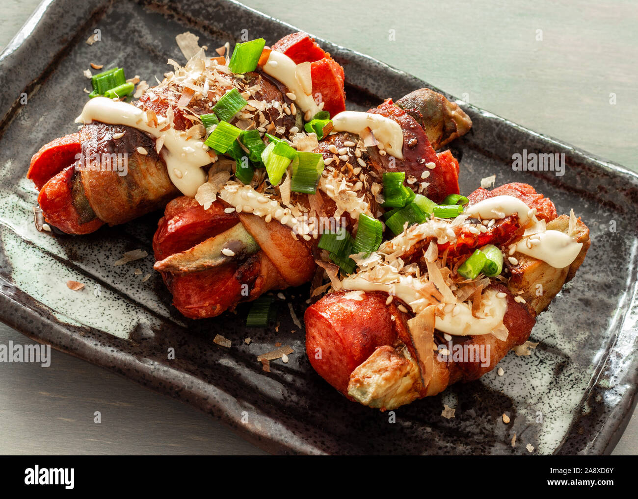 Bacon wrapped avocado hot dogs. Topped with mayo, spring onion, sesame ...