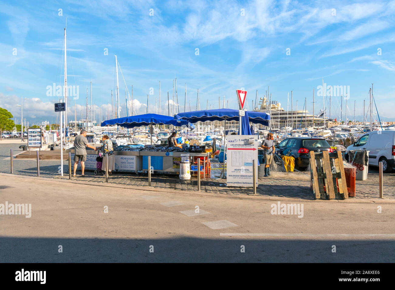 Local fishermen at a food booth sell fresh fish with a full harbor of ...