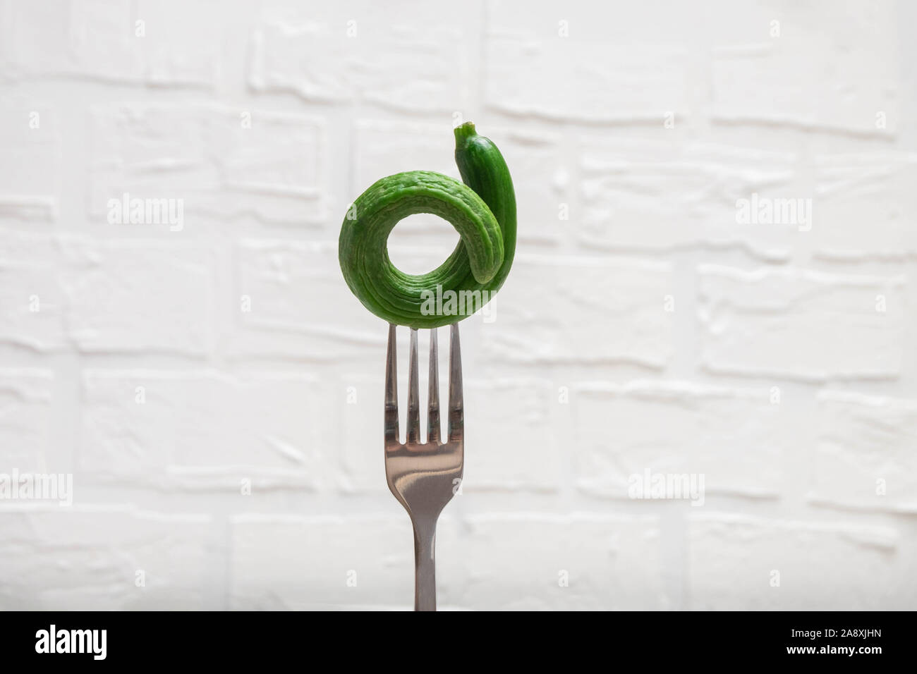 Ugly organic cucumber on silver fork on white background. Food waste ...