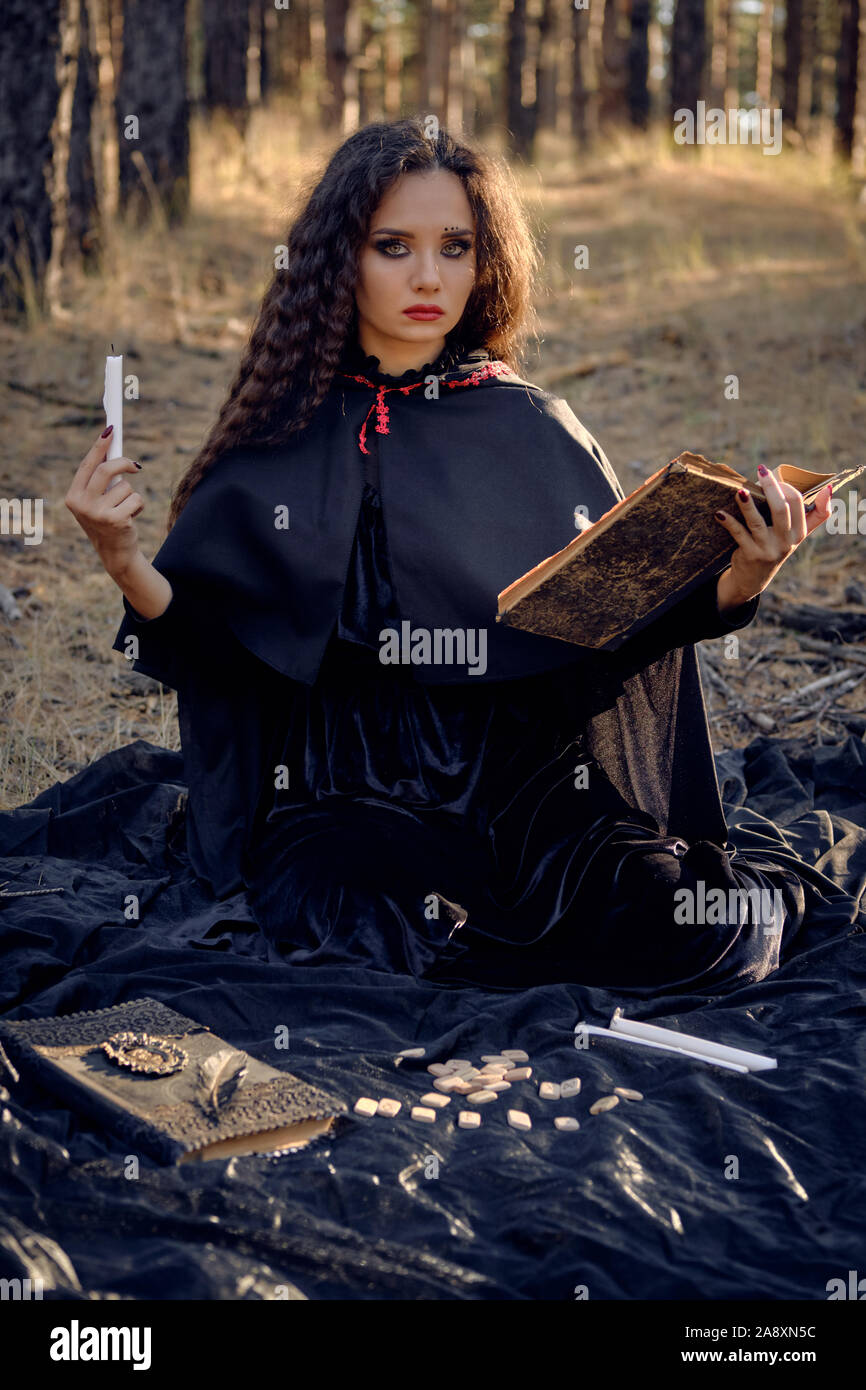 Pretty, wicked, long-haired witch in a black, long dress with cape and ...