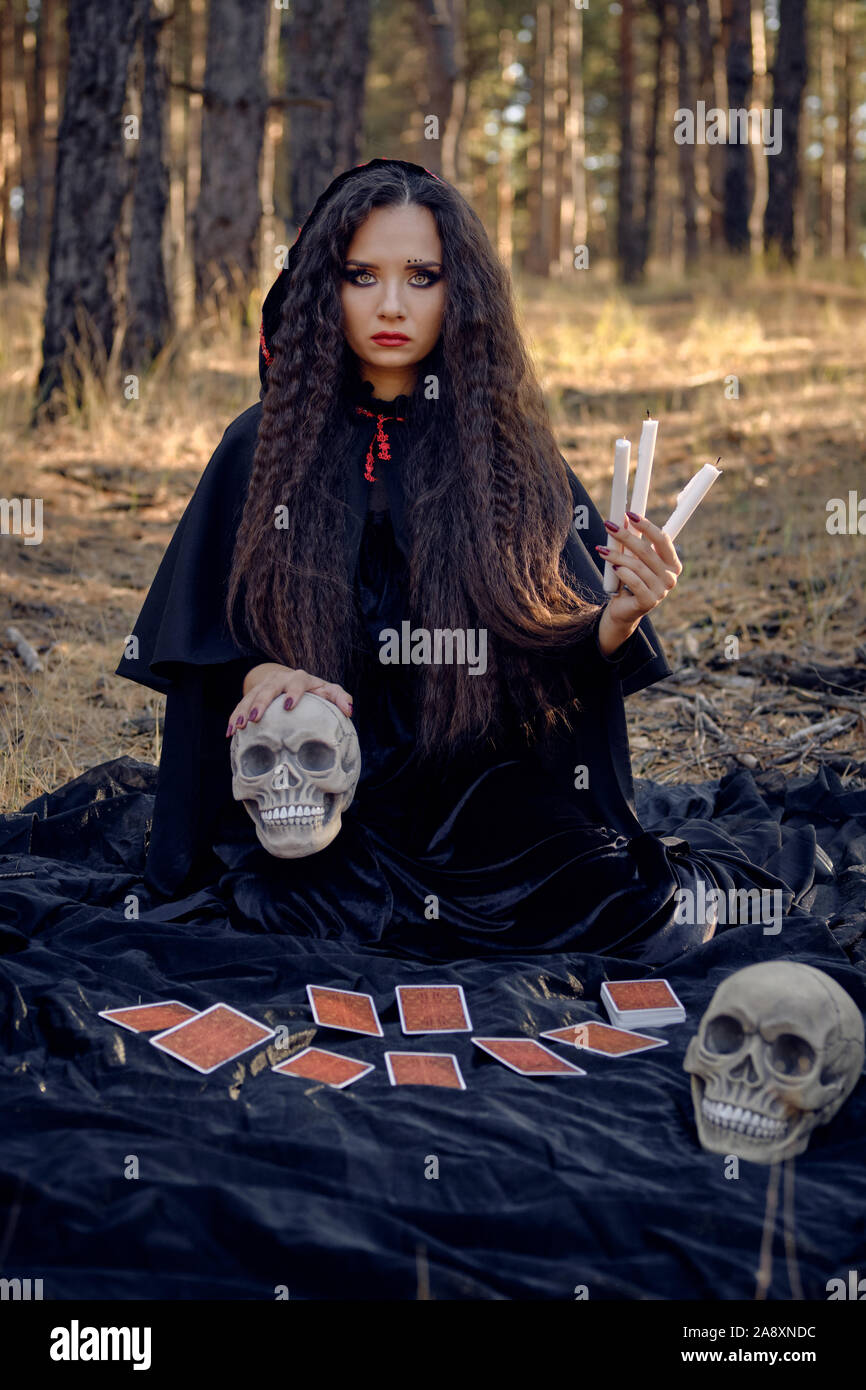 Cute, wicked, long-haired witch in a black, long dress with cape and ...