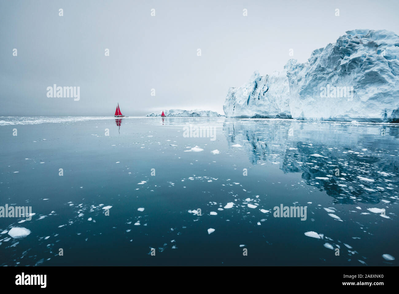 Beautiful red sailboat in the arctic next to a massive iceberg showing ...