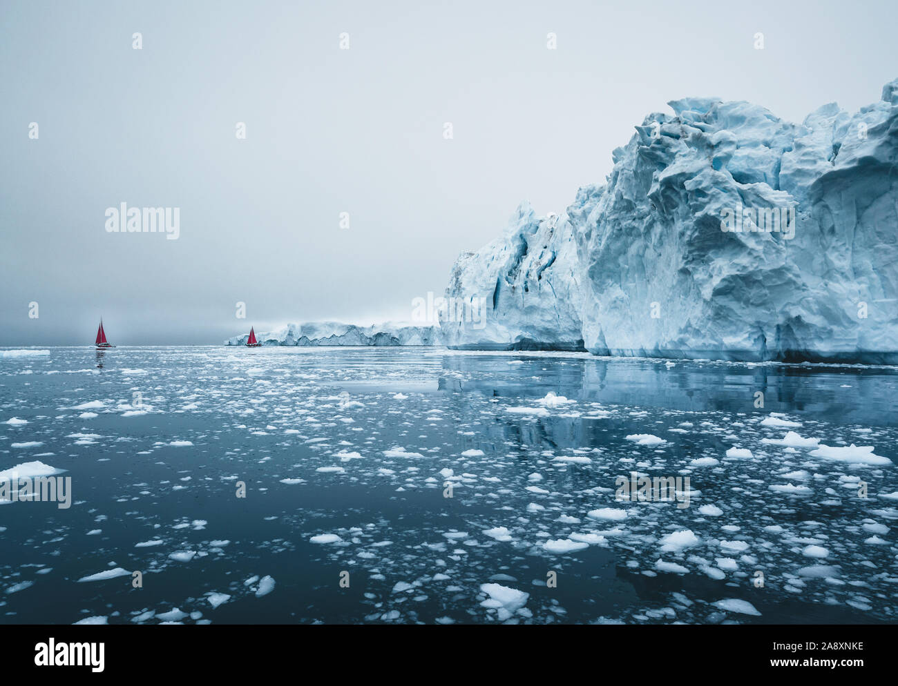Beautiful red sailboat in the arctic next to a massive iceberg showing ...