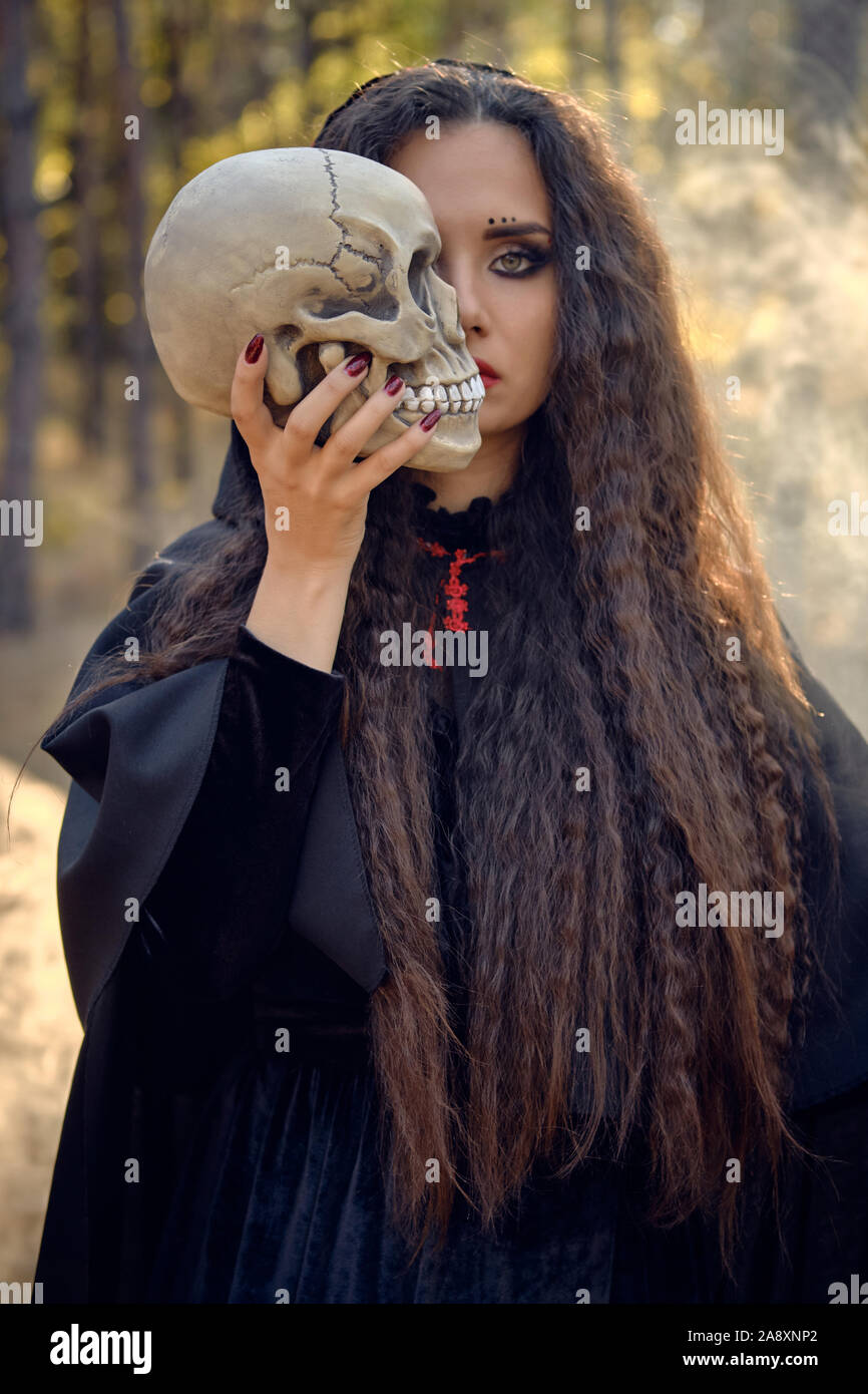 Attractive, wicked, long-haired witch in a black, long dress with cape ...