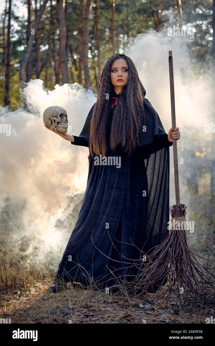 Charming, wicked, long-haired witch in a black, long dress with cape ...